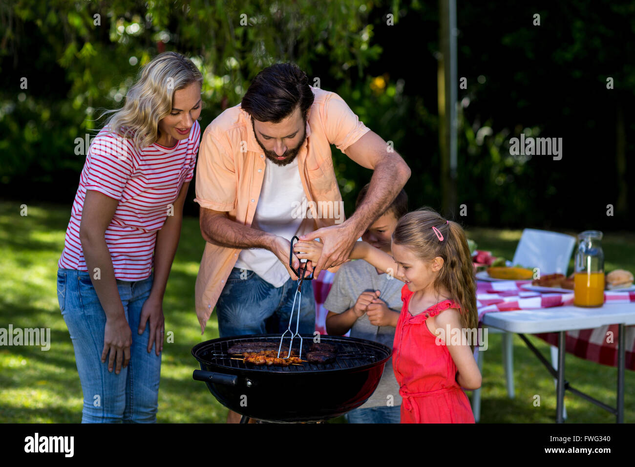 Father with mother teaching children to barbecue food Stock Photo - Alamy