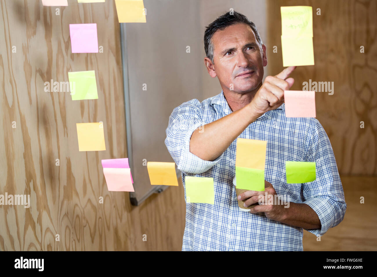 Thoughtful man reading at sticky notes while having coffee Stock Photo ...