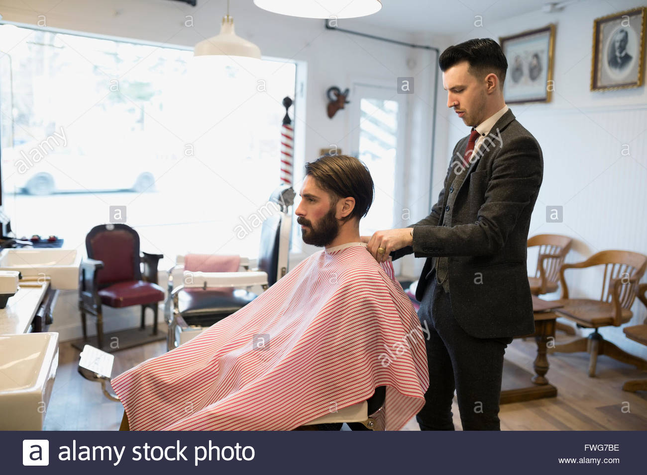 Barber fastening smock on customer in barber shop Stock Photo - Alamy