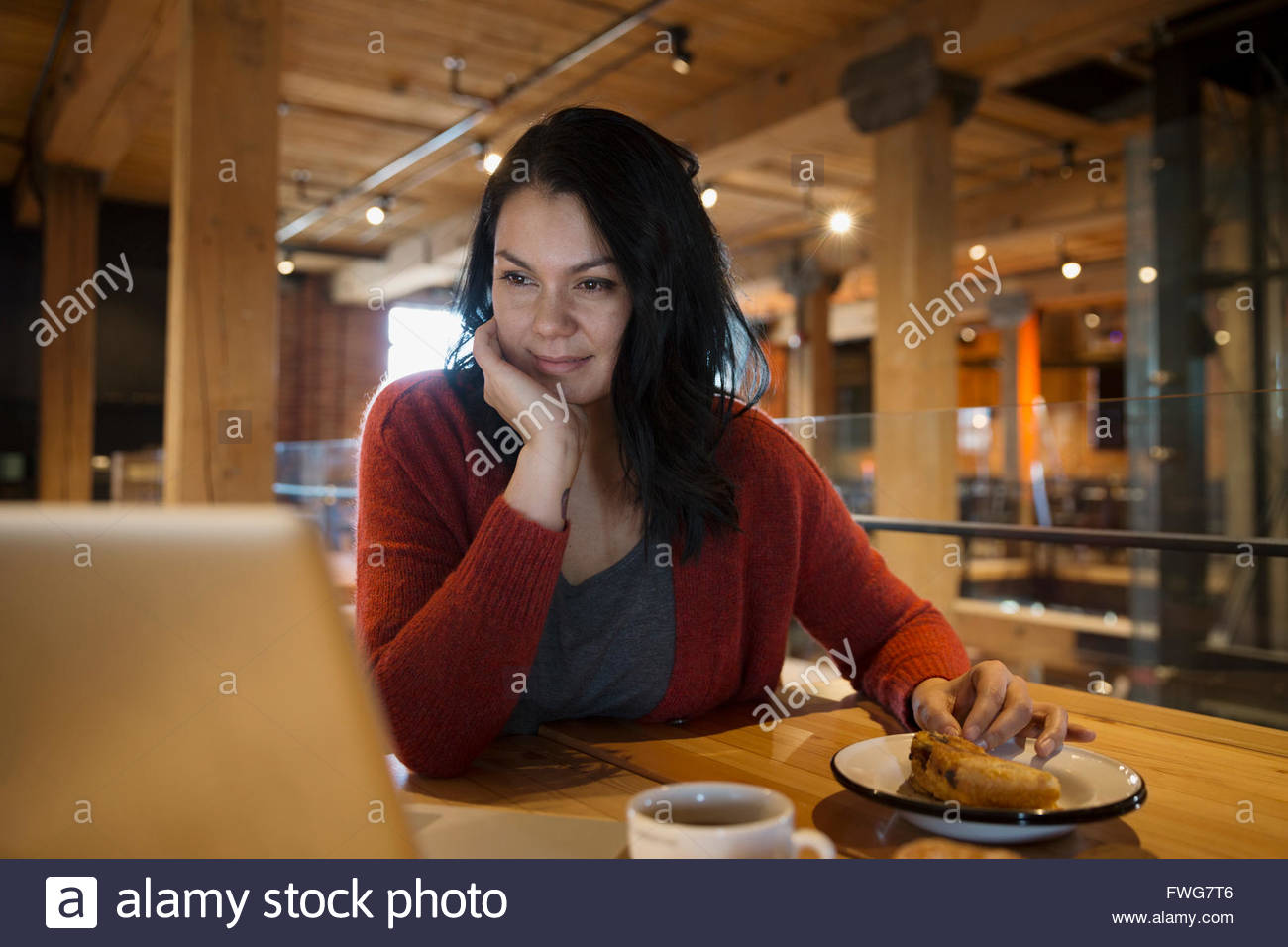 Woman eating pastry at laptop in bakery Stock Photo - Alamy