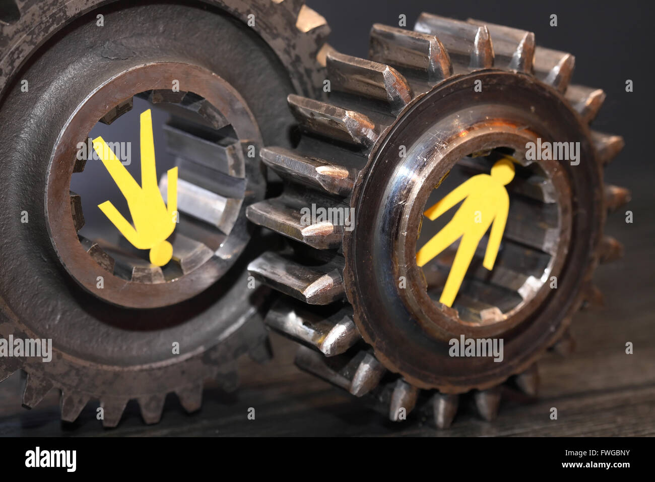 Yellow paper men inside old metal gears on dark background Stock Photo ...