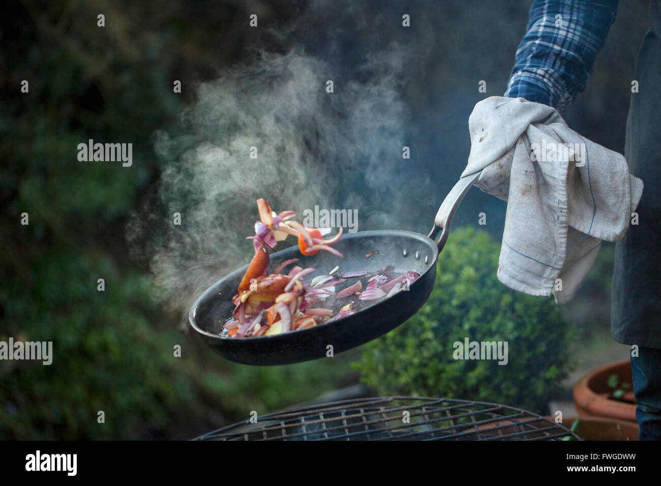 An outdoor cookout. A man holding a frying pan sauteeing vegetables ...