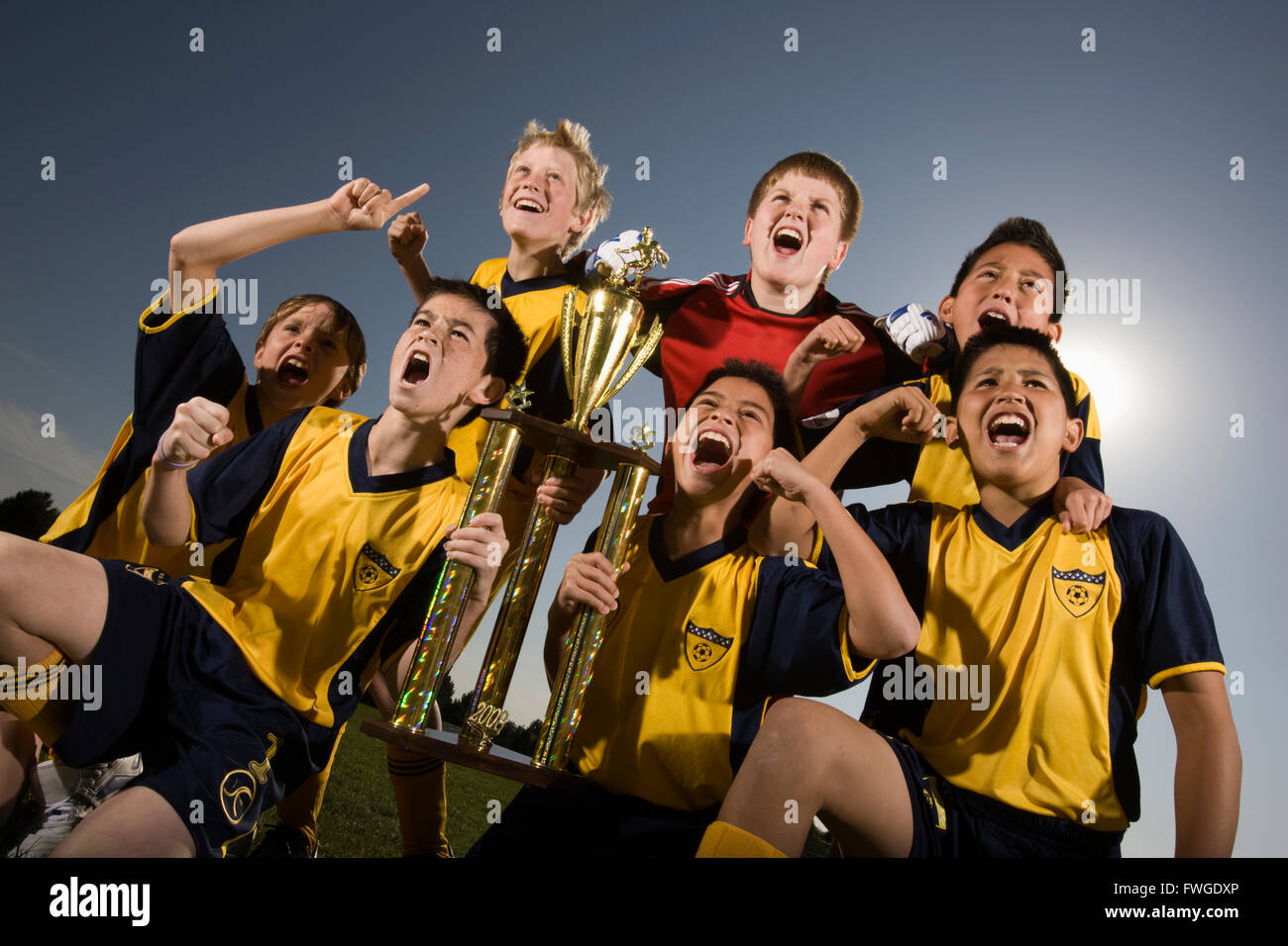 A group of boys in soccer team shirts holding a trophy and celebrating ...