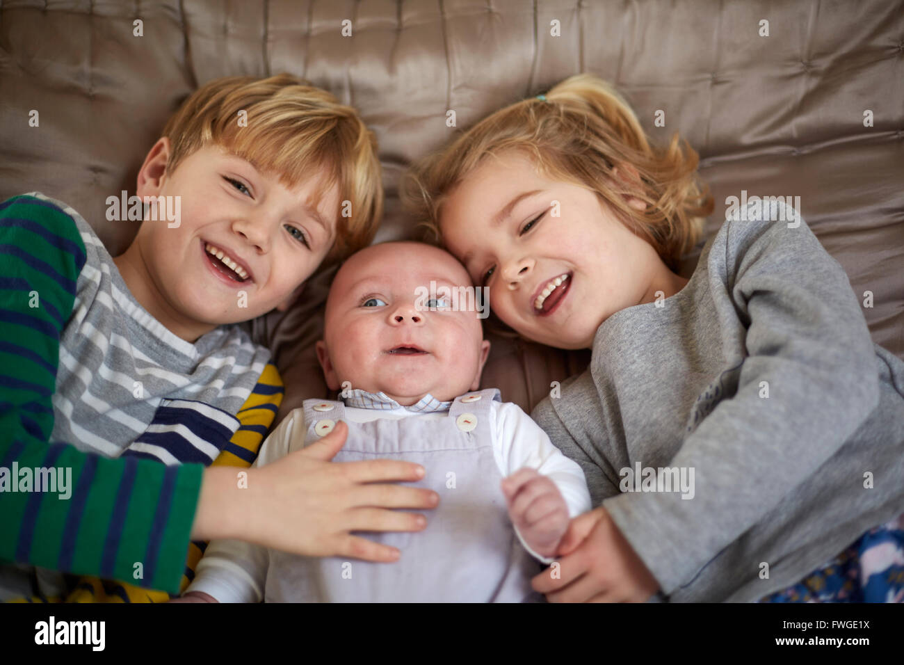 Three children lying on a bed, a boy and girl with a baby between them ...