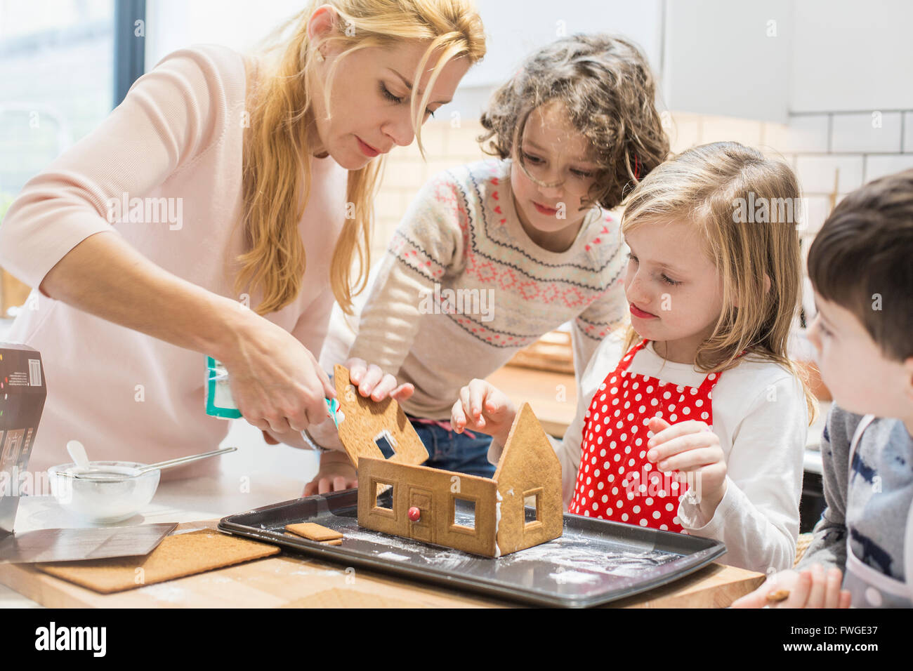 A woman and three children creating a baked gingerbread house Stock ...