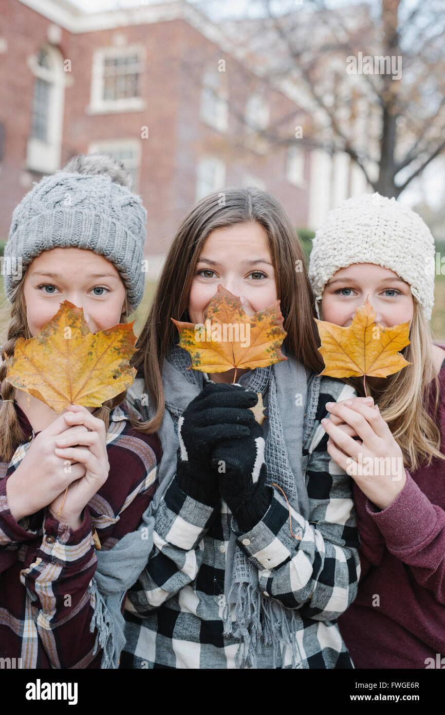 Three young girls standing in a row, holding autumn leaves in front of ...