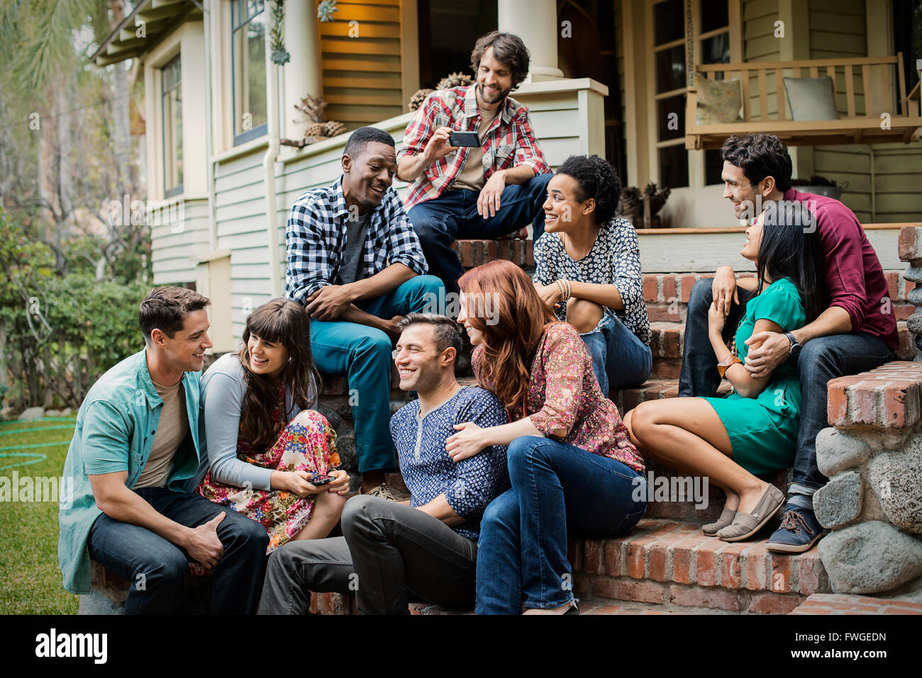 A group of friends sitting on the steps of a house porch, talking and ...