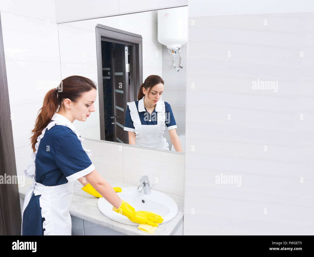 Reflection of female housekeeping worker wearing yellow rubber gloves ...