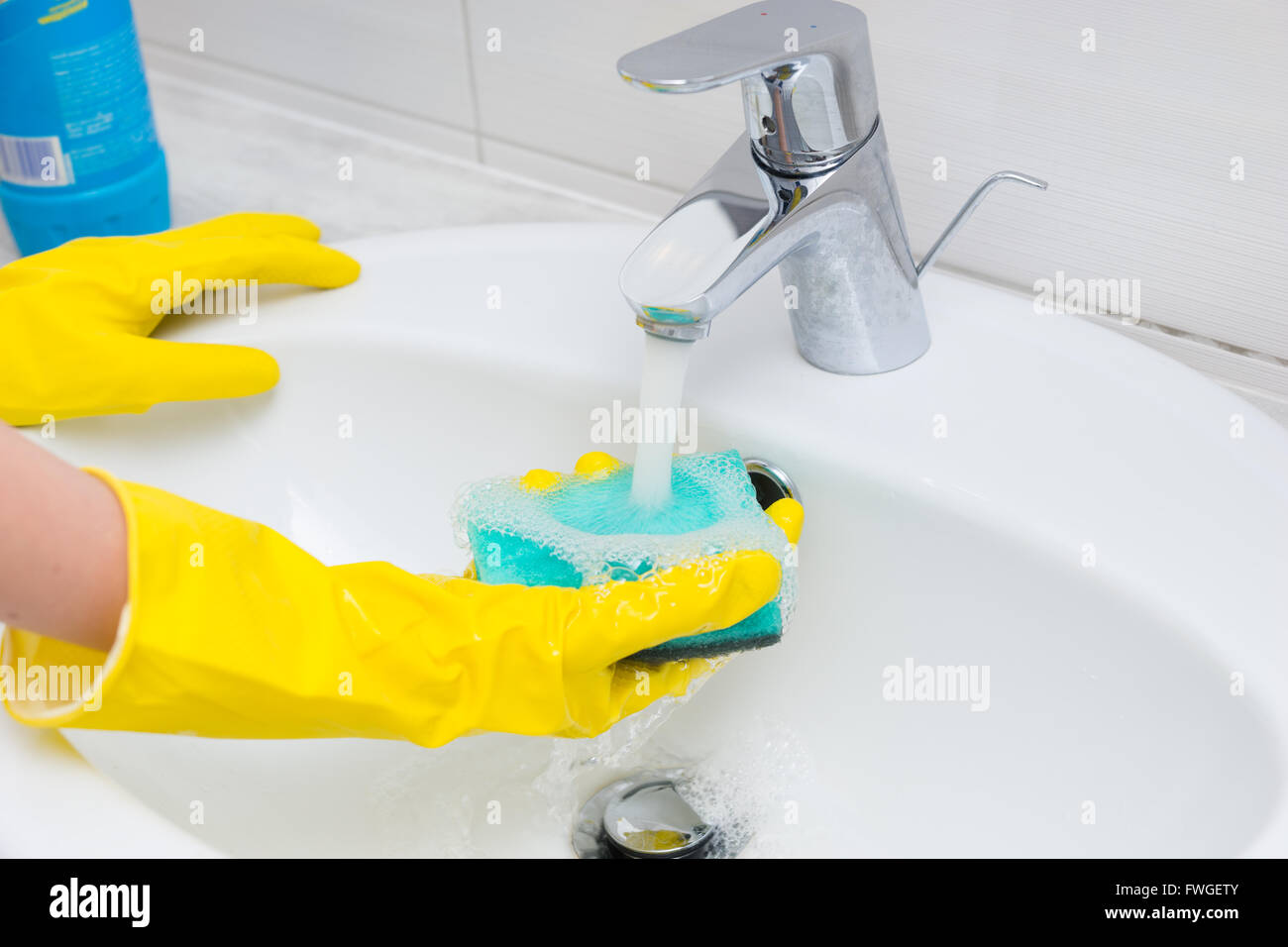 Housewife washing the hand basin in the bathroom with her gloved hands ...