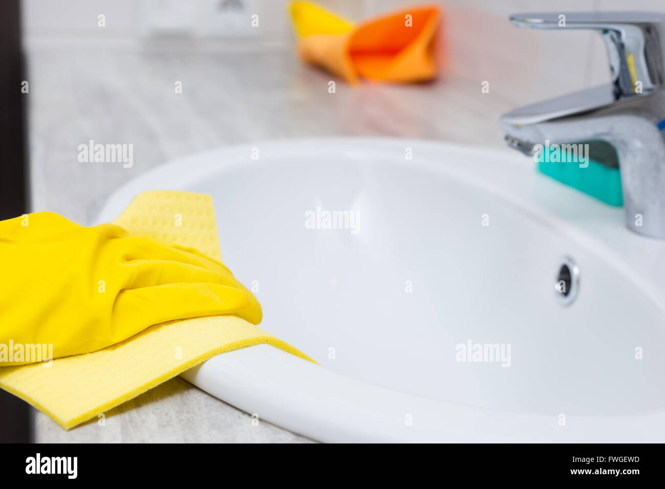 Close up view on yellow rubber gloved hand cleaning edge of ivory sink ...
