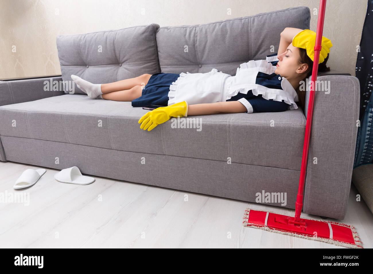 Exhausted housekeeper relaxing on the job lying on a couch in her ...