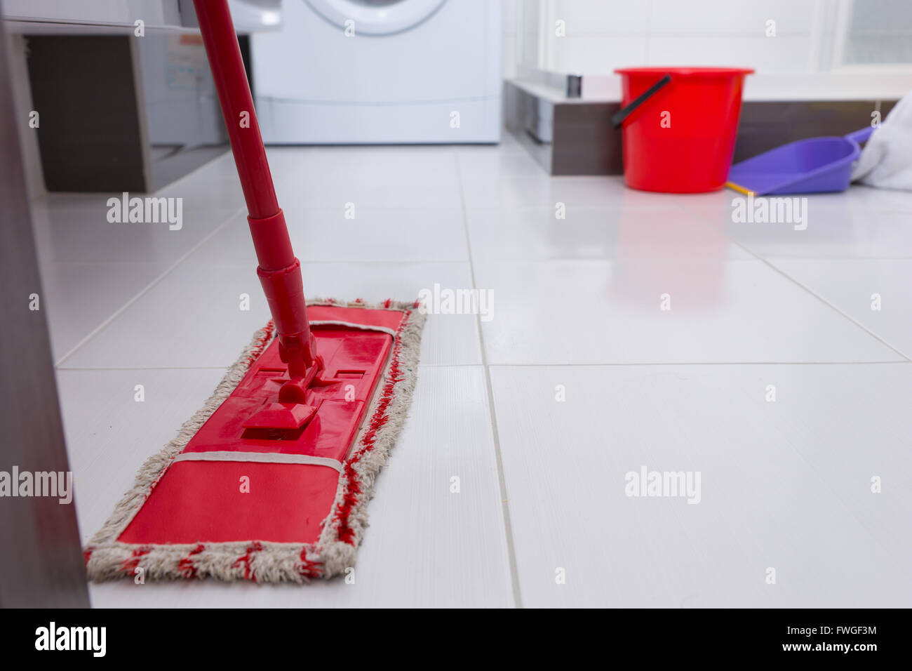 Colorful red mop on a clean white tiled floor with a washing machine ...