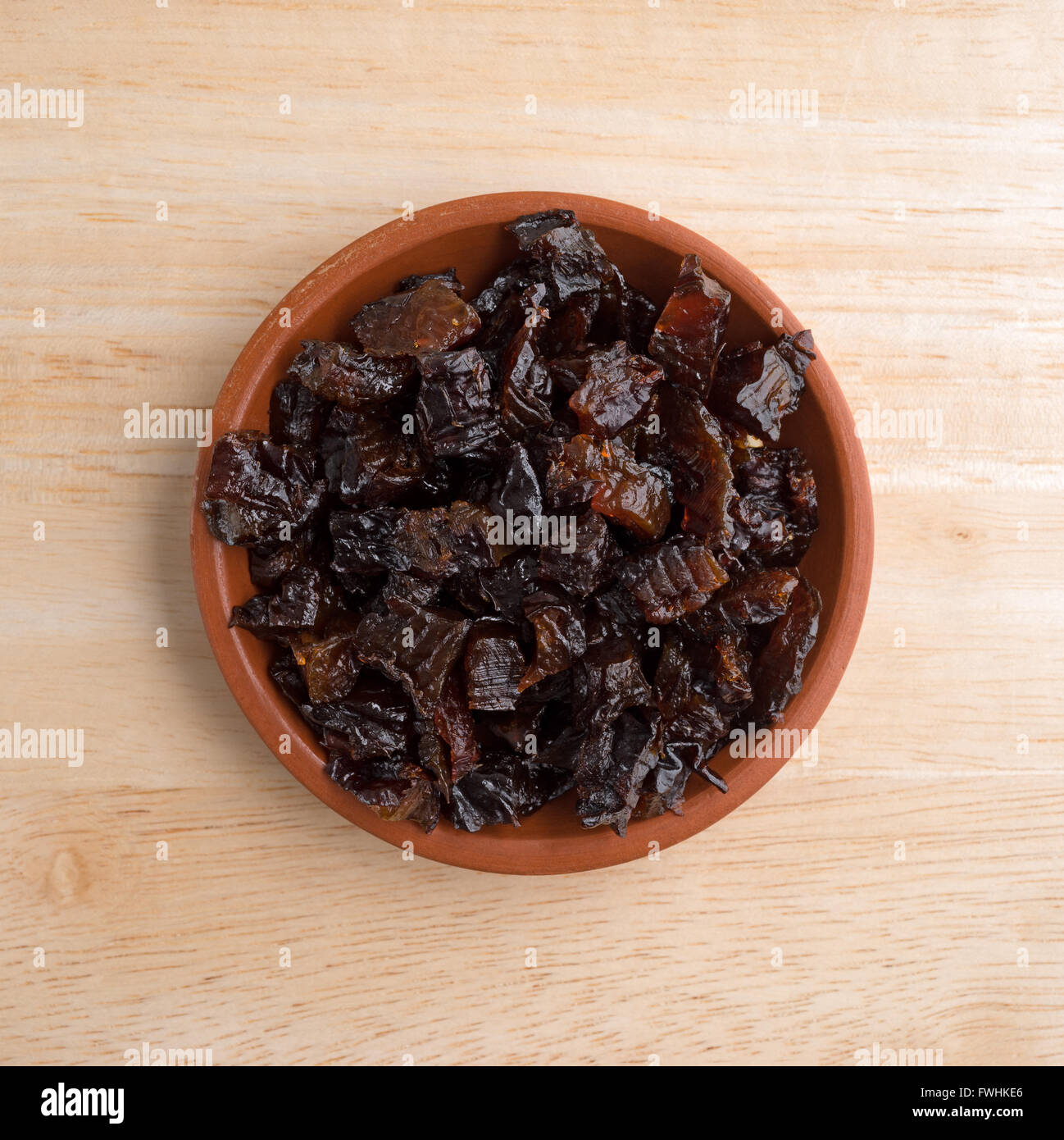 Top view of a portion of diced prunes in a small bowl atop a wood table ...
