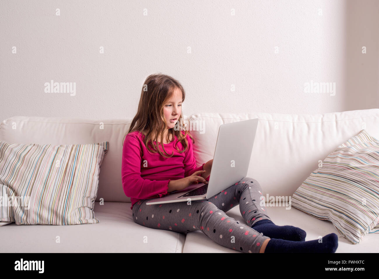 Girl at home sitting on sofa, playing with laptop Stock Photo - Alamy