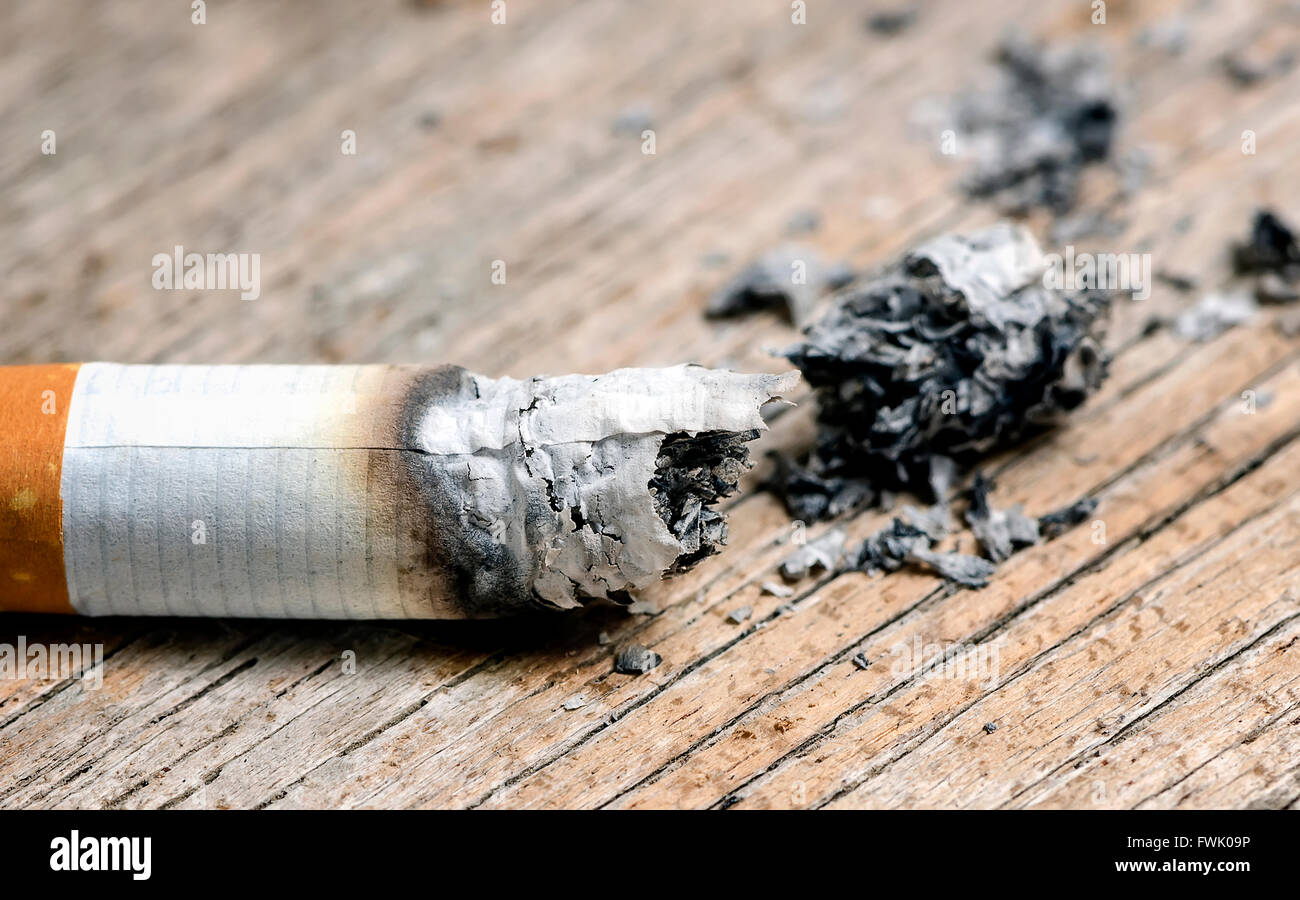 Cigarette burned and cigarette ashes on wooden background Stock Photo - Alamy