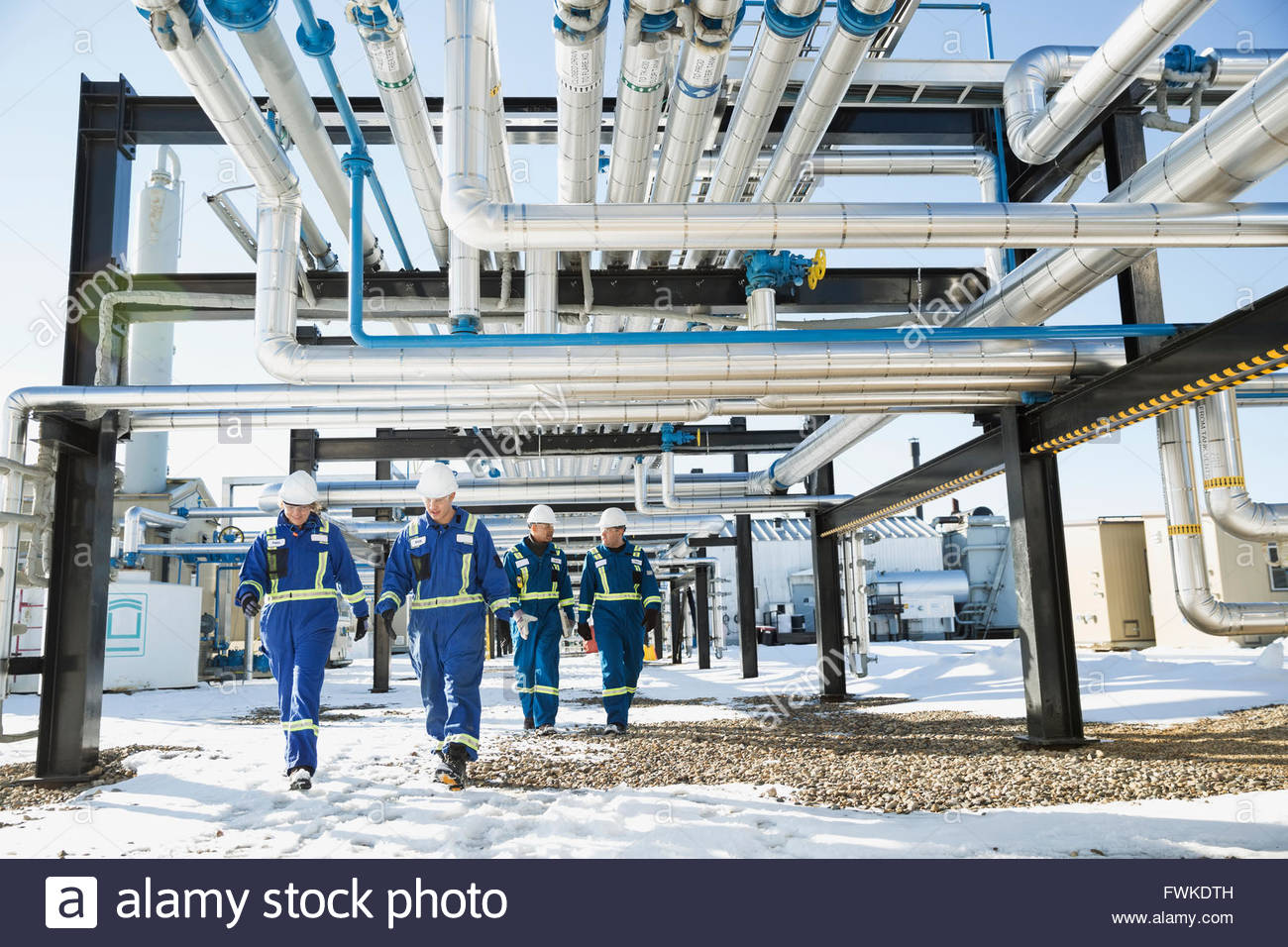 Workers walking in snow below gas plant pipelines Stock Photo - Alamy
