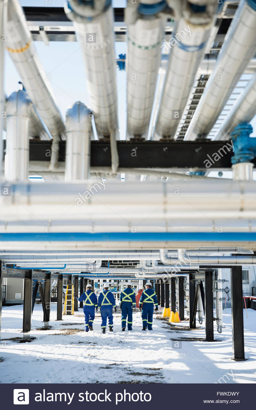 Workers walking in snow below gas plant pipelines Stock Photo - Alamy