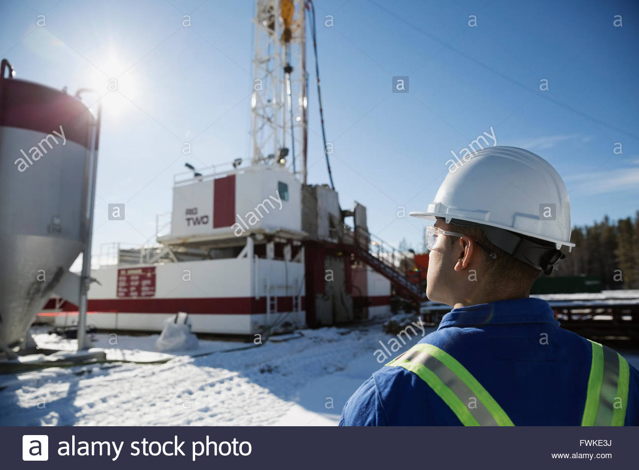 Male worker looking up at drilling rig snow Stock Photo - Alamy