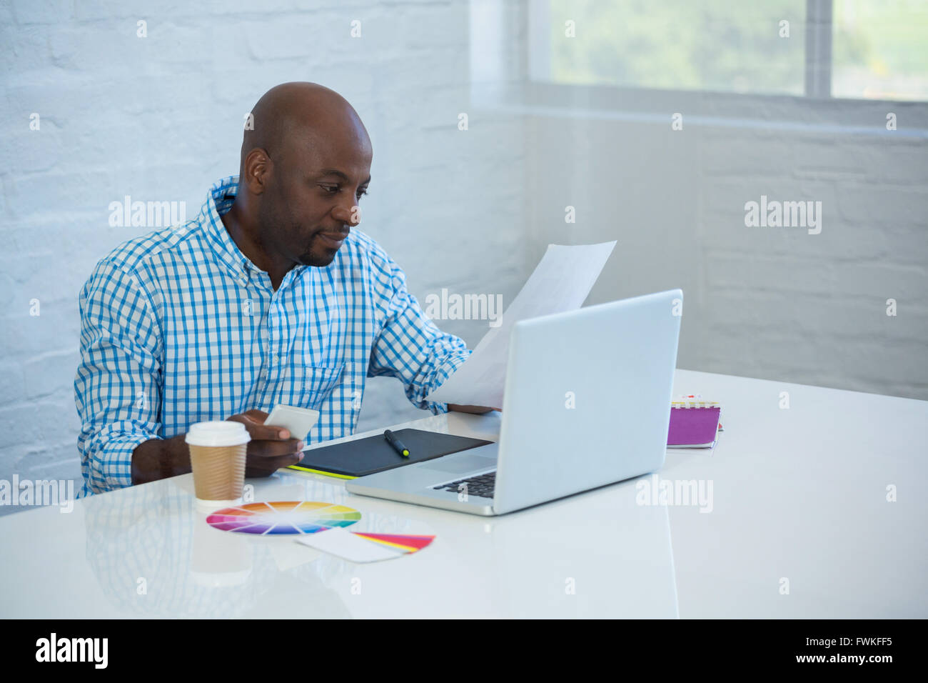 Graphic designer reading a document with laptop on table Stock Photo ...