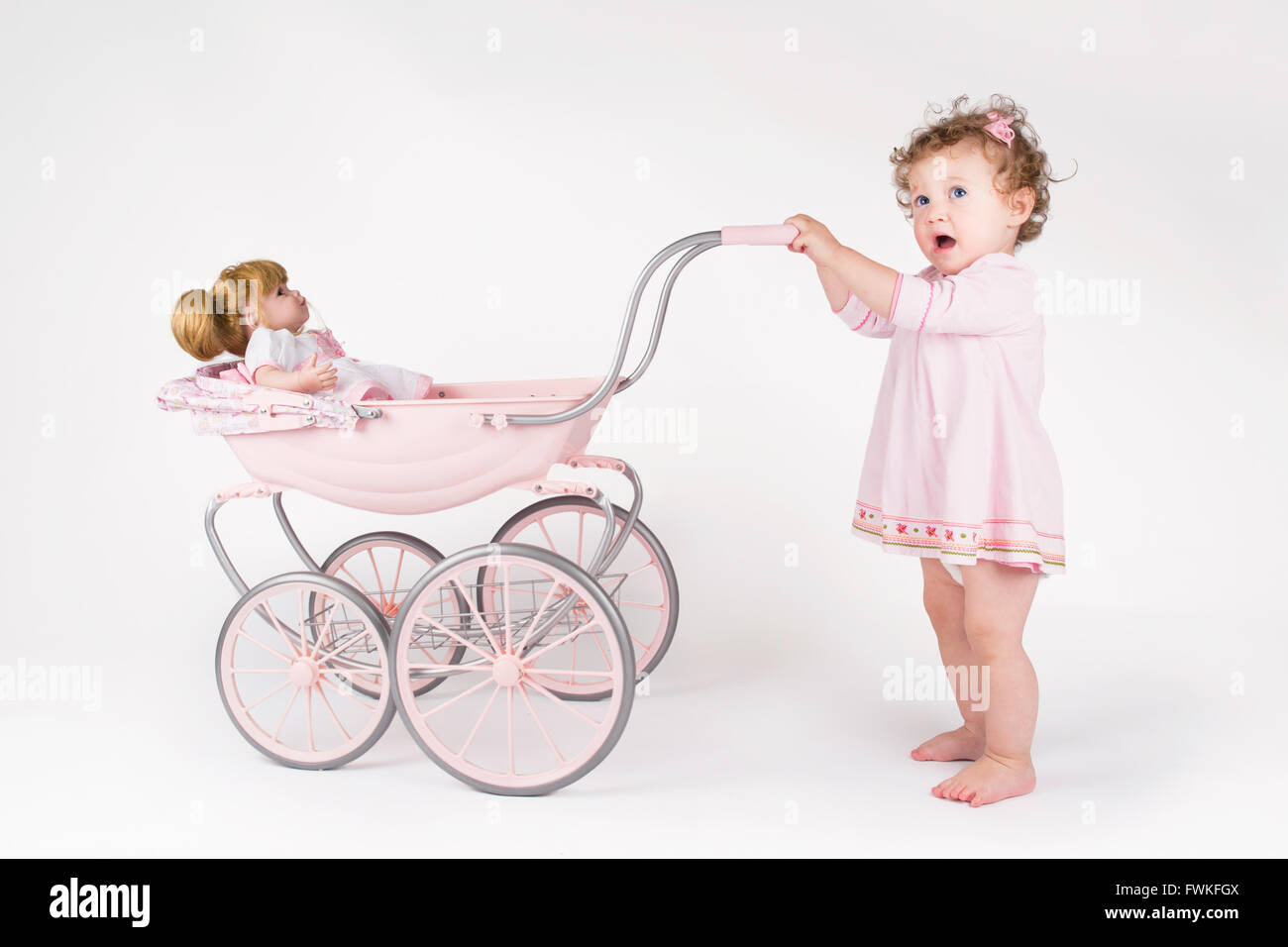 Funny baby girl walking with a doll stroller Stock Photo - Alamy