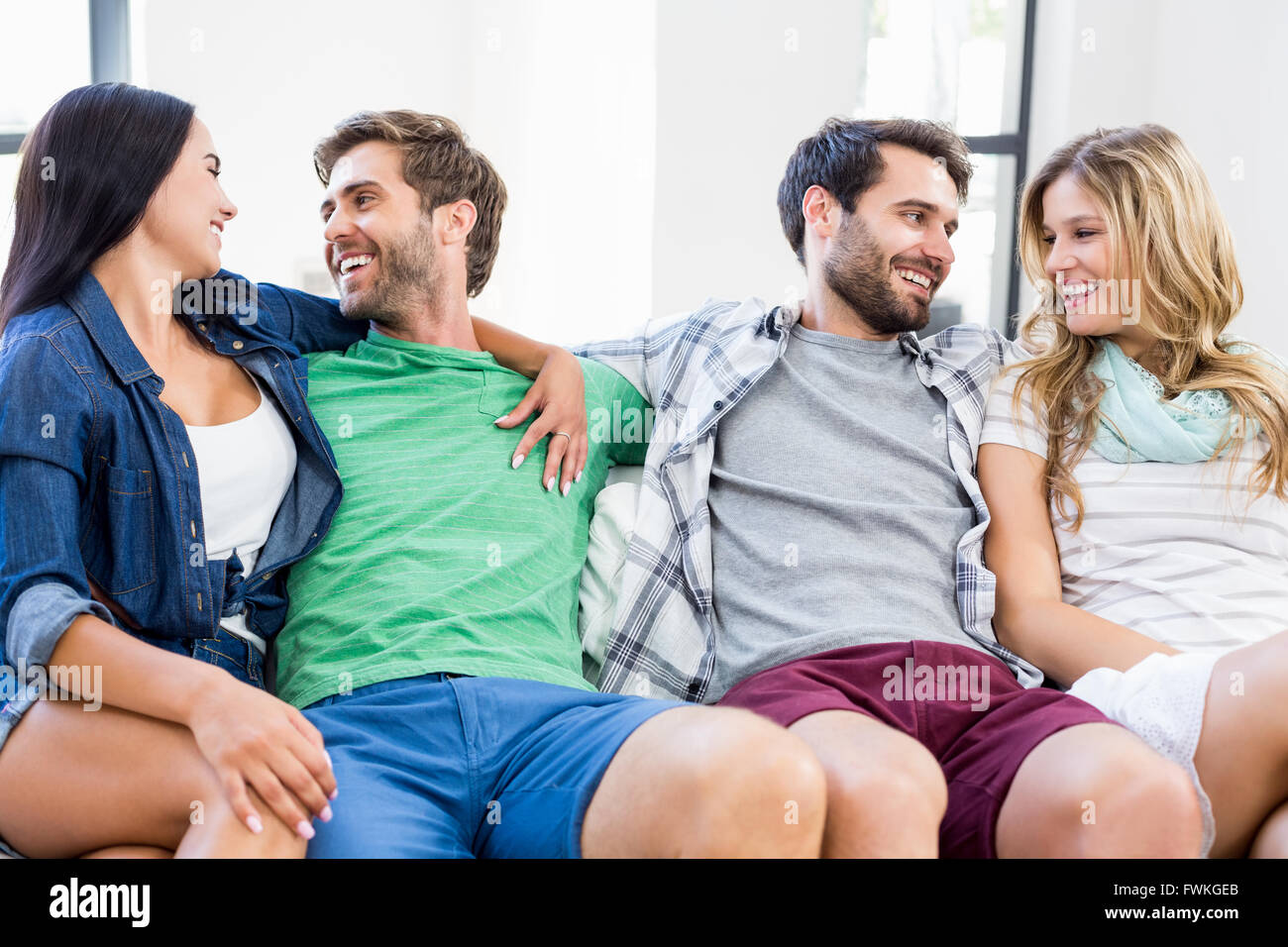 Happy friends sitting on sofa and talking Stock Photo - Alamy