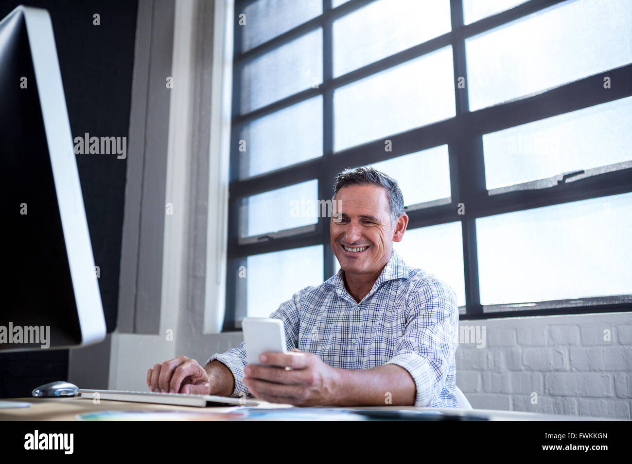 Man text messaging on mobile phone while using computer Stock Photo - Alamy