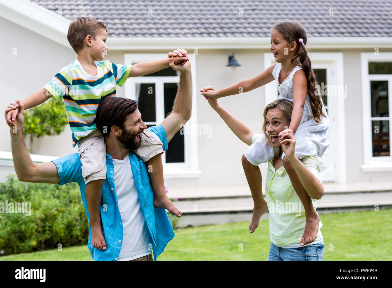 Parents carrying children on shoulder in yard Stock Photo - Alamy