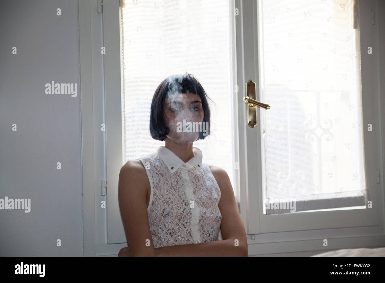 Young woman standing window smoking hi-res stock photography and images ...