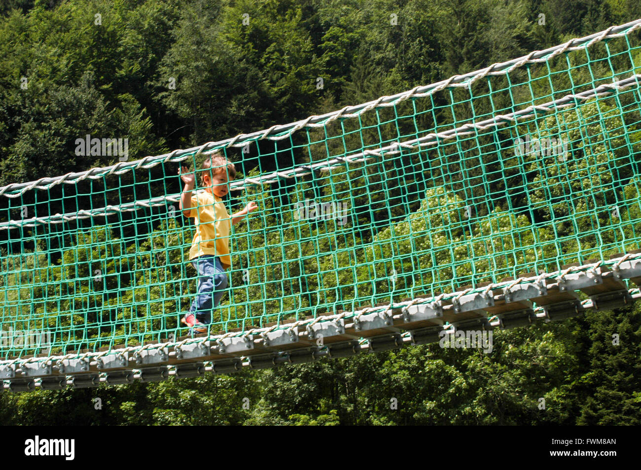 Happy child crossing over suspension bridge in playground on sunny day ...