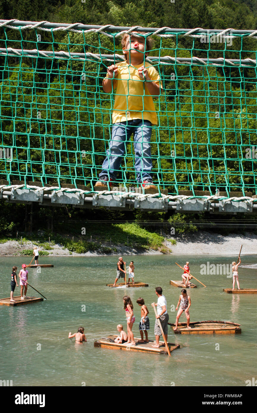 Happy child crossing over suspension bridge in playground on sunny day ...