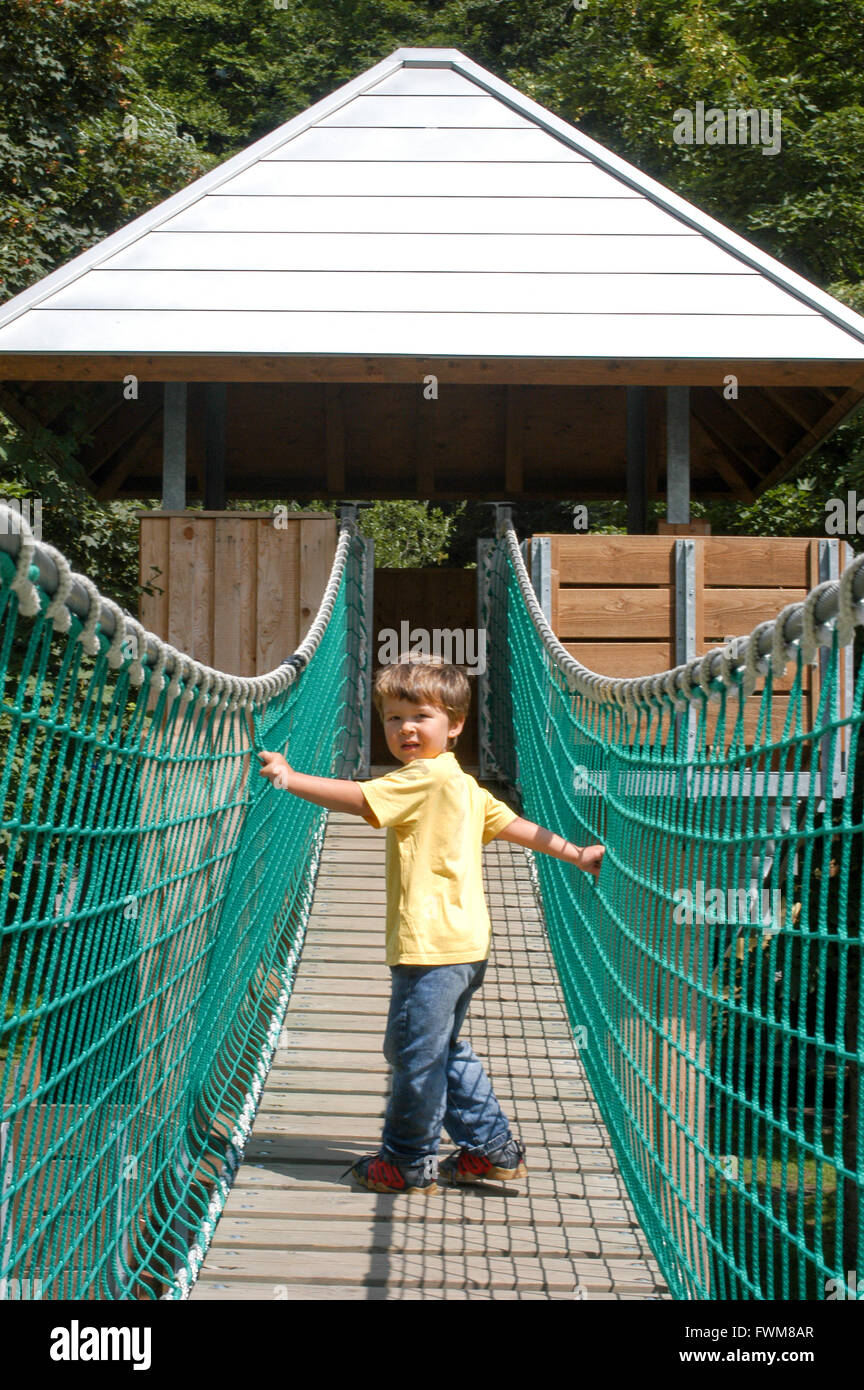 Happy child crossing over suspension bridge in playground on sunny day ...