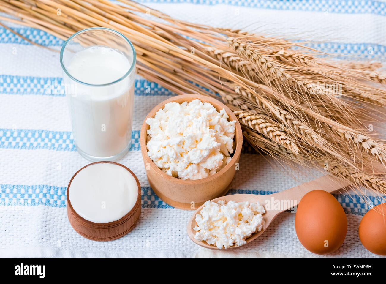 Cottage cheese, glass of milk, two eggs, wooden spoon with cottage ...