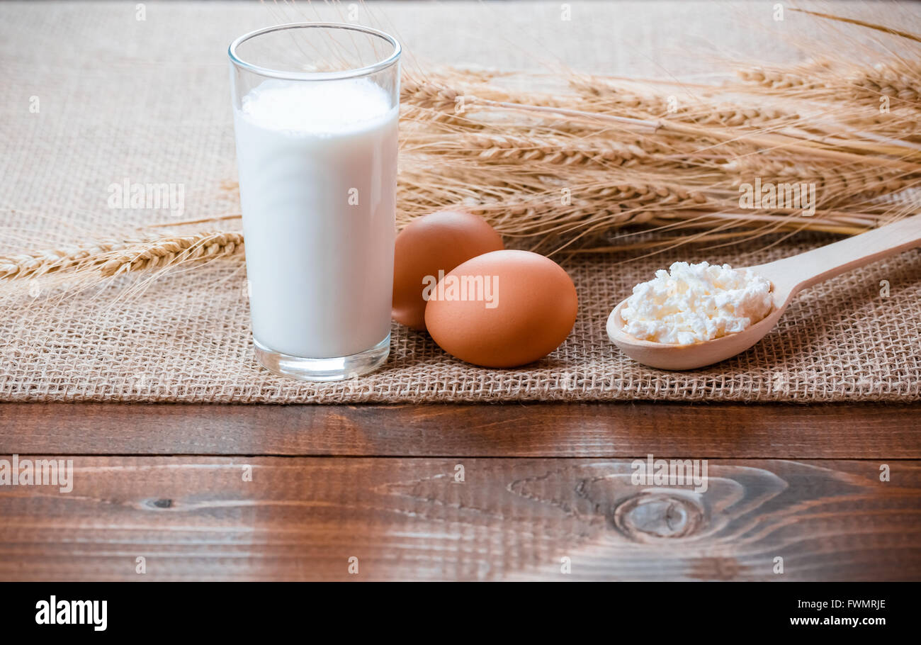 Cottage cheese, glass of milk, two eggs, wooden spoon with cottage ...