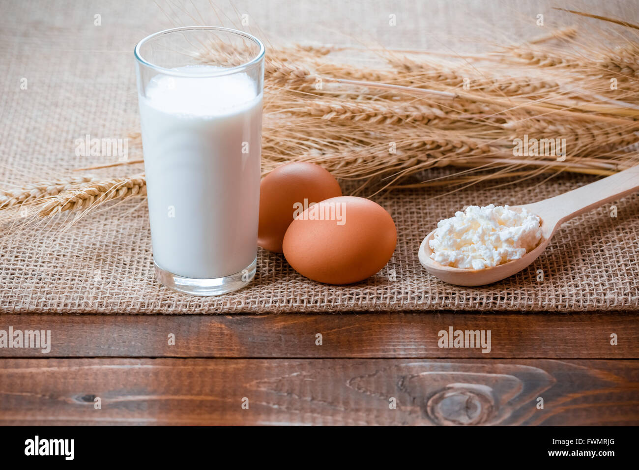 Cottage cheese, glass of milk, two eggs, wooden spoon with cottage ...
