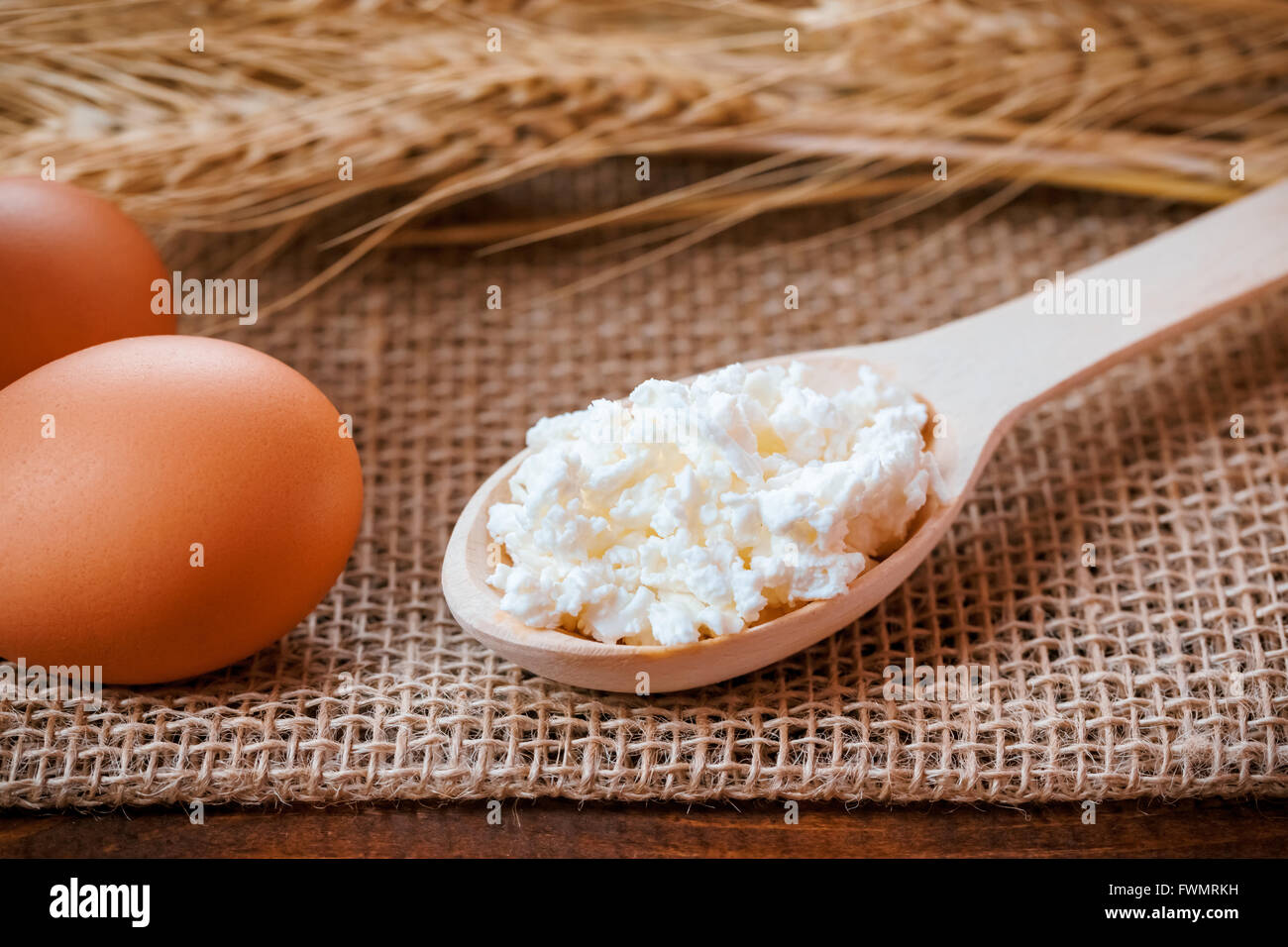 Two eggs, wooden spoon with cottage cheese and wheat ears lie on the ...
