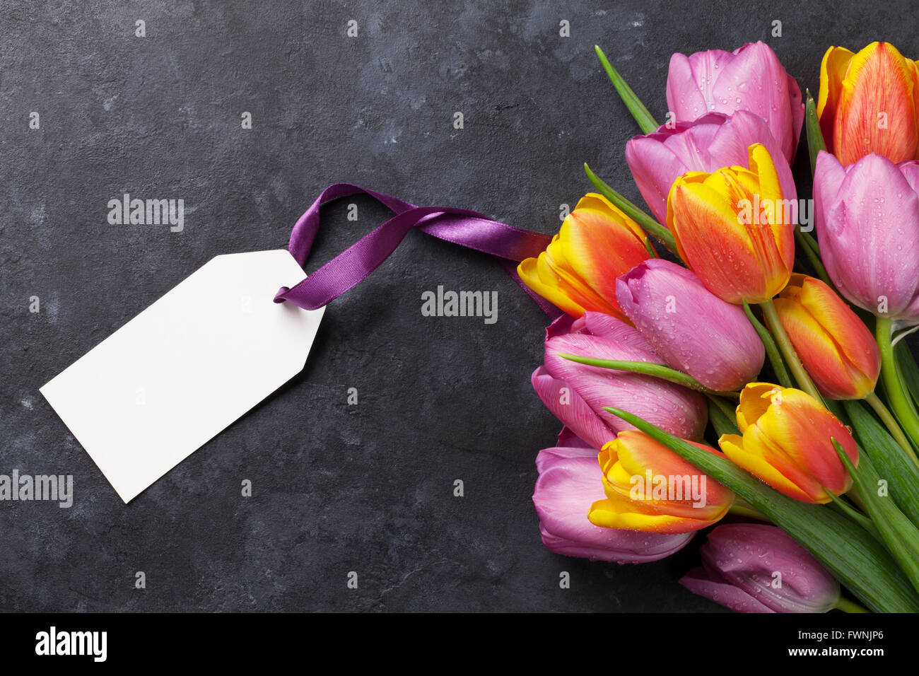 Fresh colorful tulip flowers with tag label on dark stone table. Top ...