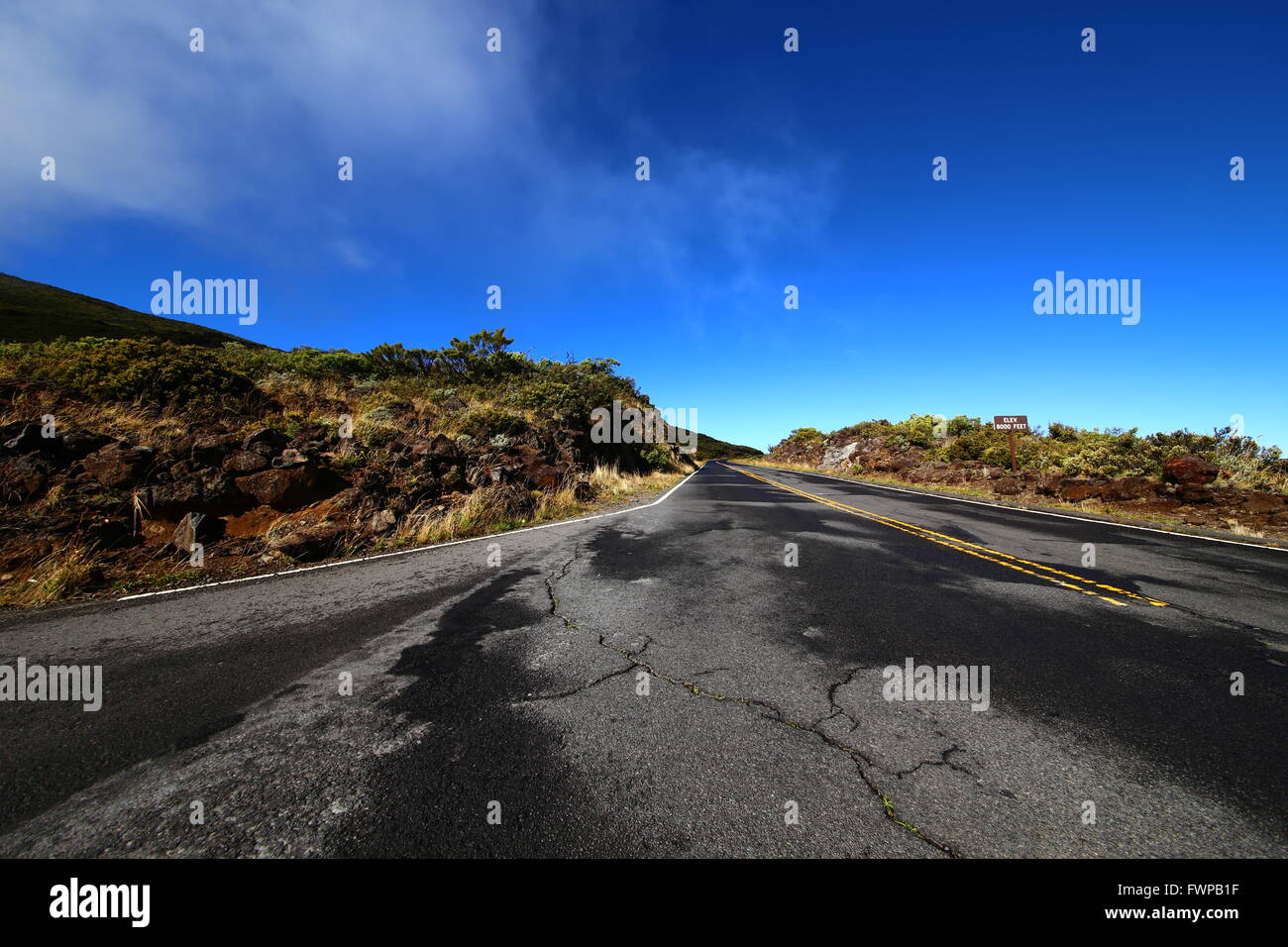 Cracked tarmacked road leading up a hill into blue sky Stock Photo - Alamy