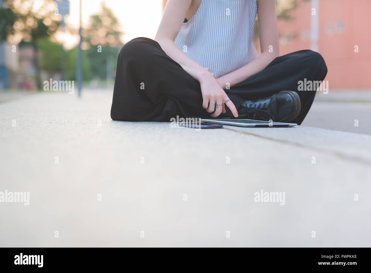 From the neck down view of young beautiful woman sitting on a sidewalk ...
