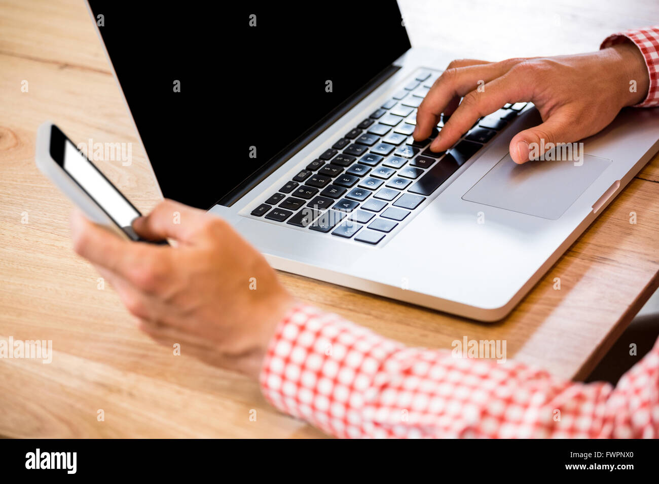 Man text messaging on mobile phone while using laptop Stock Photo - Alamy