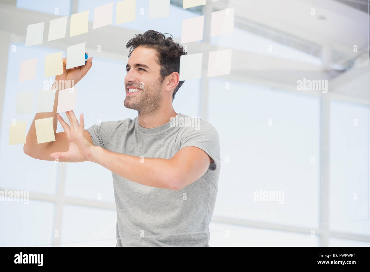 Smiling man writing on sticky notes on window Stock Photo - Alamy
