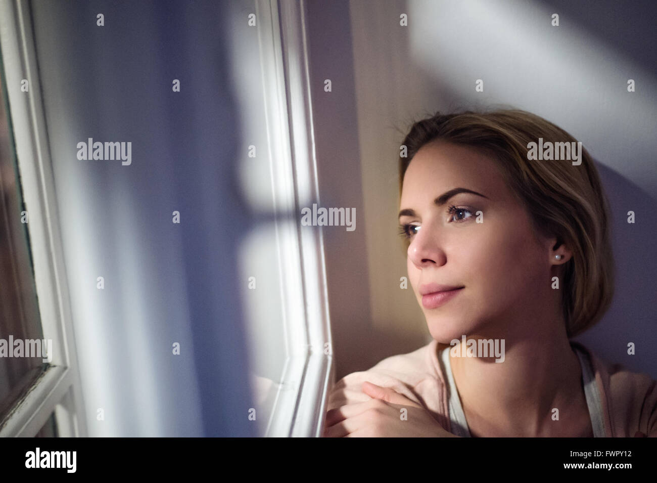 Woman sitting on window sill, looking out of window Stock Photo - Alamy