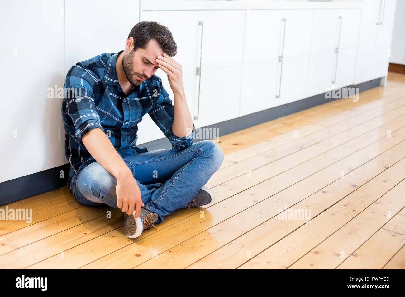 Tensed man with hand on forehead sitting on wooden floor Stock Photo ...