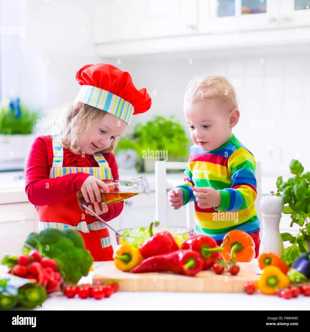 Kids cooking fresh vegetable salad in a white kitchen. Children cook ...