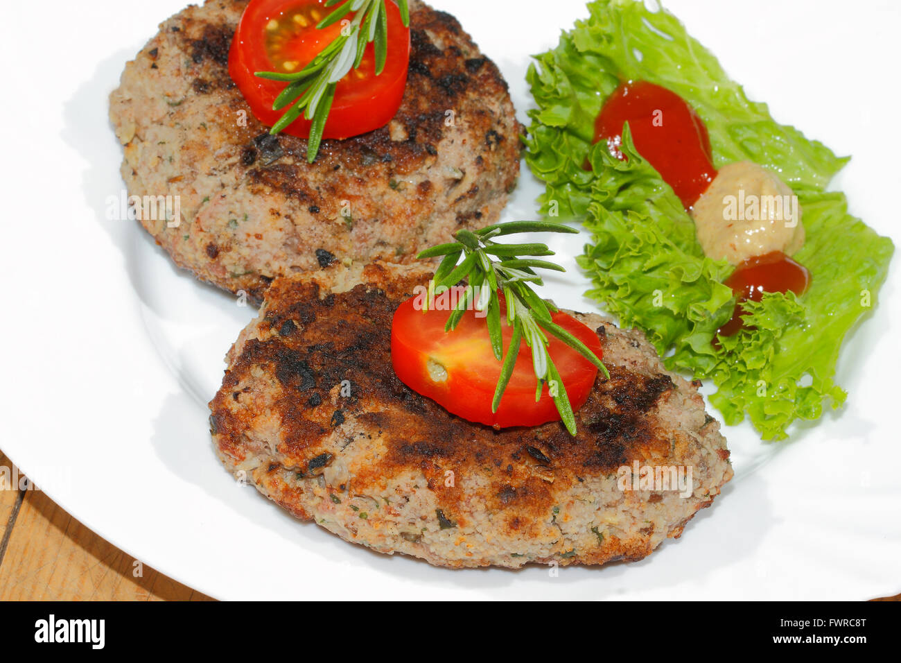Grilled beef patties, garnished with sliced tomato and rosemary ...