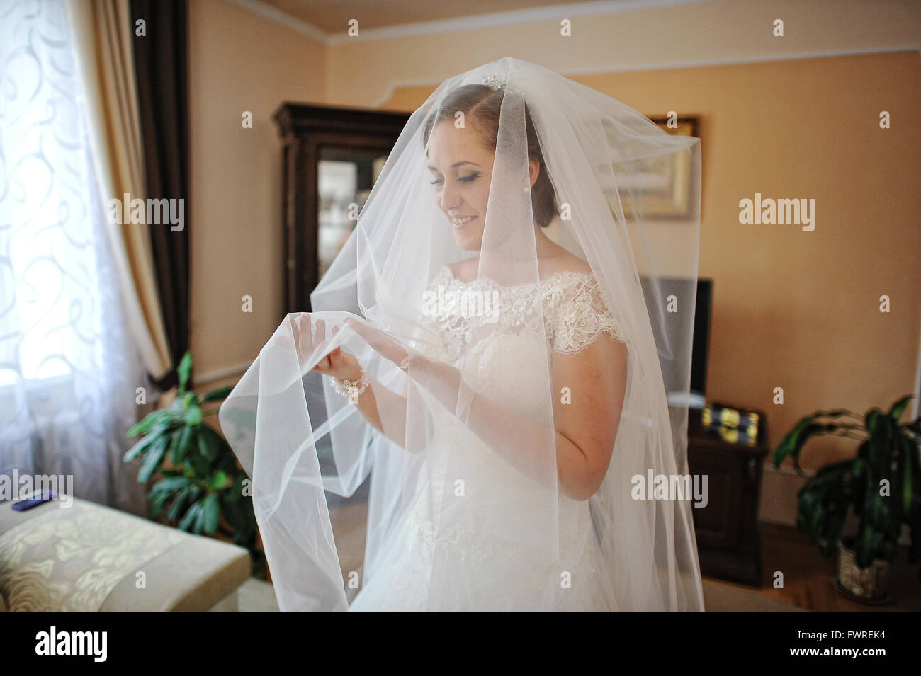 Charming smiled bride under veil stay at room and looked at her hands ...