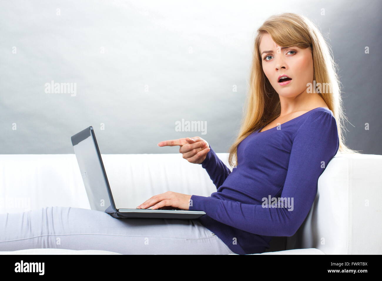 Shocked, surprised and worry woman sitting on sofa, using and showing ...