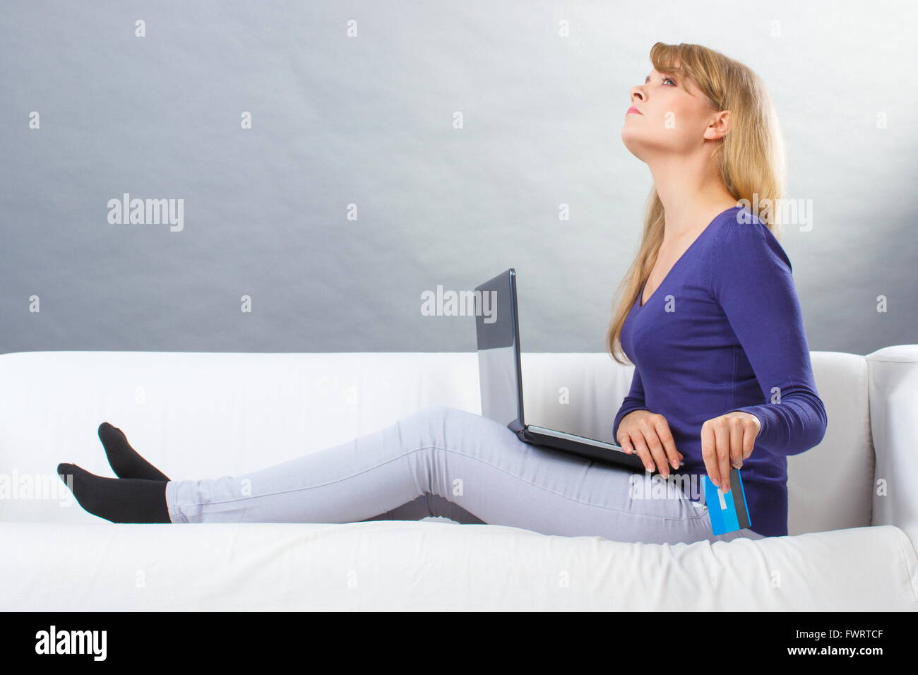 Angry woman using laptop sitting on sofa and throwing credit card ...