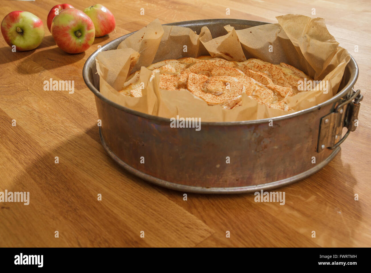 Newly baked apple pie in a metal springform with apples lying next to ...