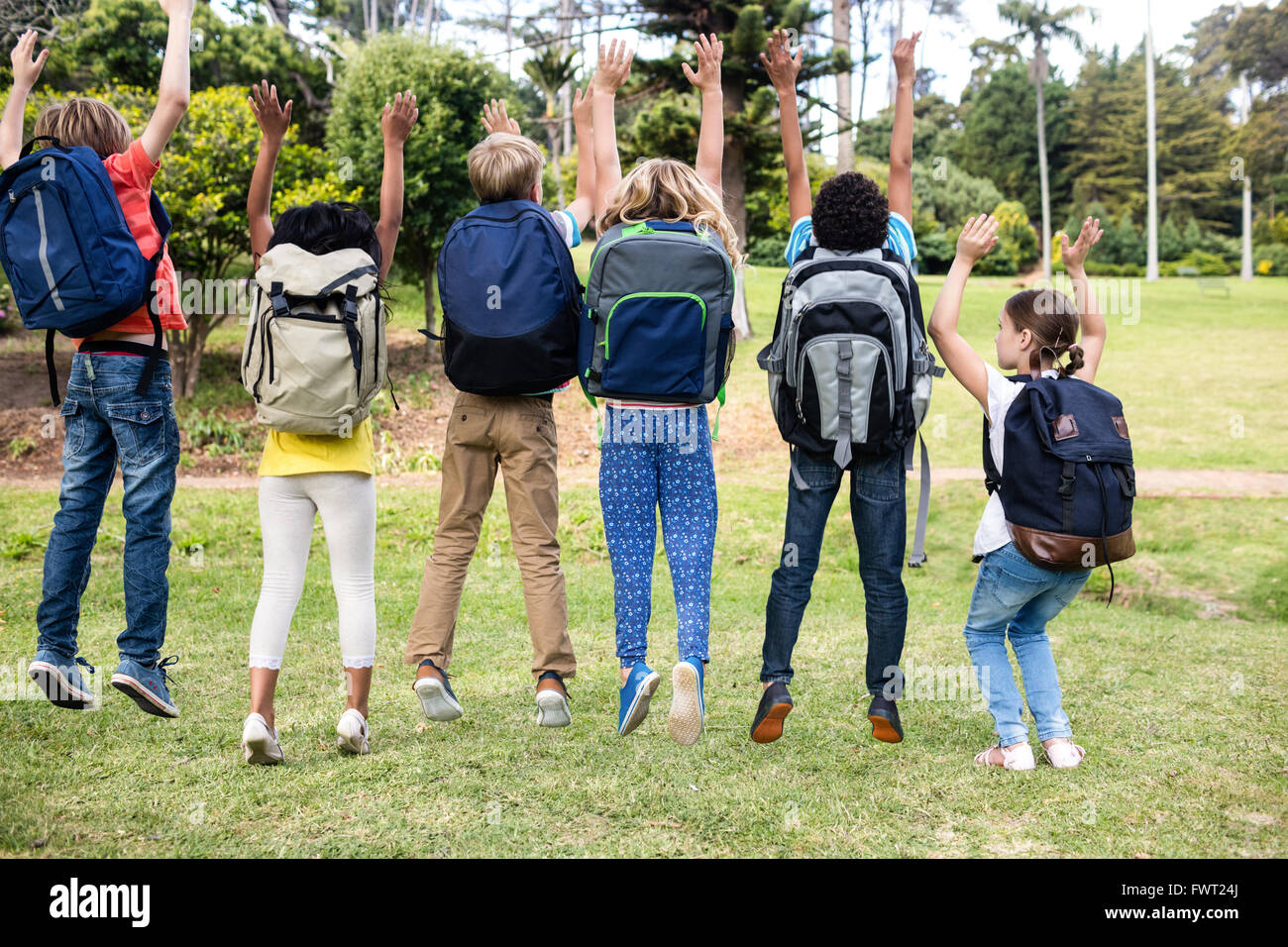 Rear view of children with bags jumping together Stock Photo - Alamy