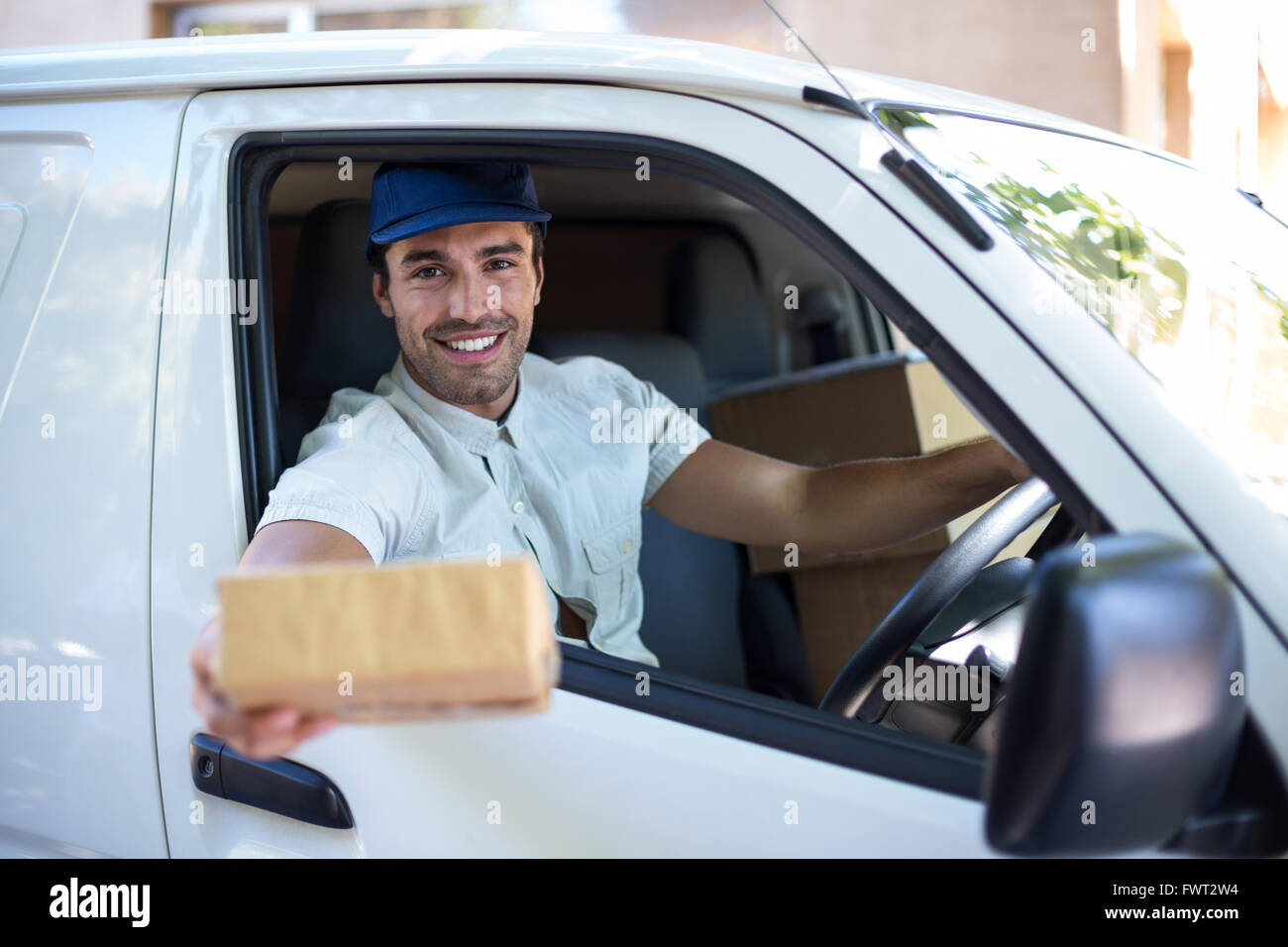 Smiling delivery man giving cardboard box Stock Photo - Alamy
